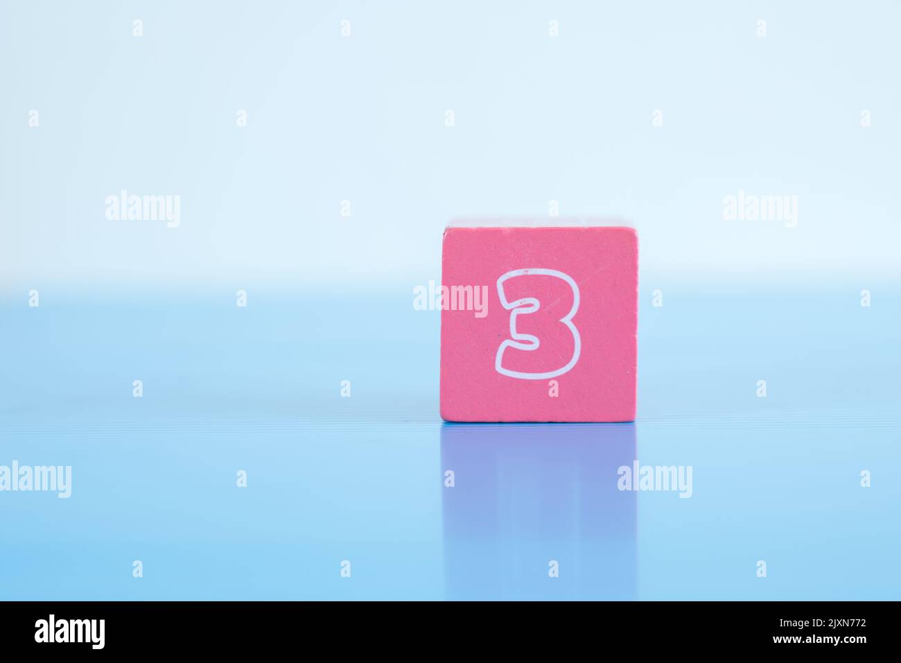 A pink cube with the number 3 on it isolated on a blue gradient ...