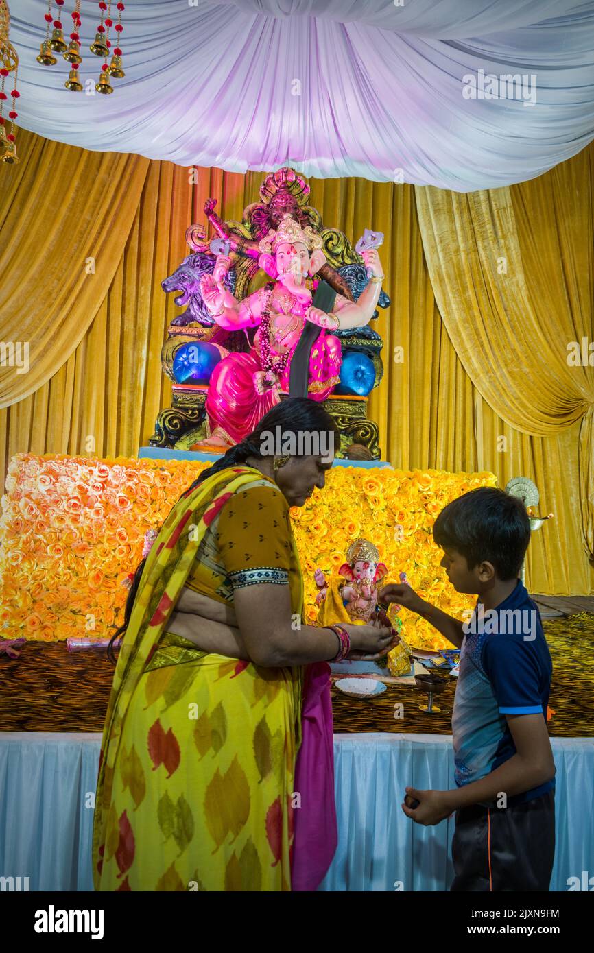 A lady taking prasad from a boy before a beautiful idol of Lord Ganesha ...