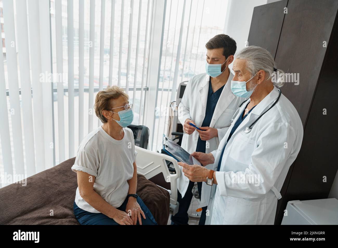 Doctors in masks explain to a sick patient in a wheelchair her ...