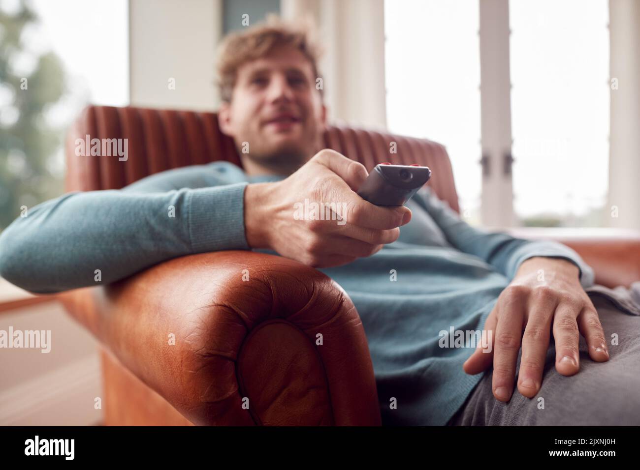 Man Sitting Relaxing On Armchair At Home Watching TV Using Remote ...
