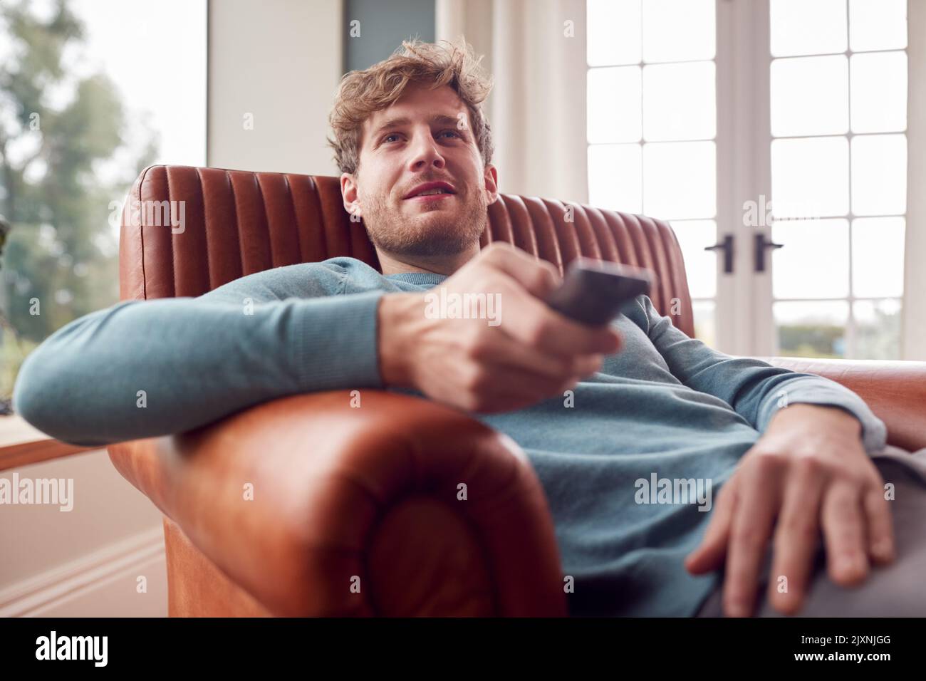 Man Sitting Relaxing On Armchair At Home Watching TV Using Remote ...