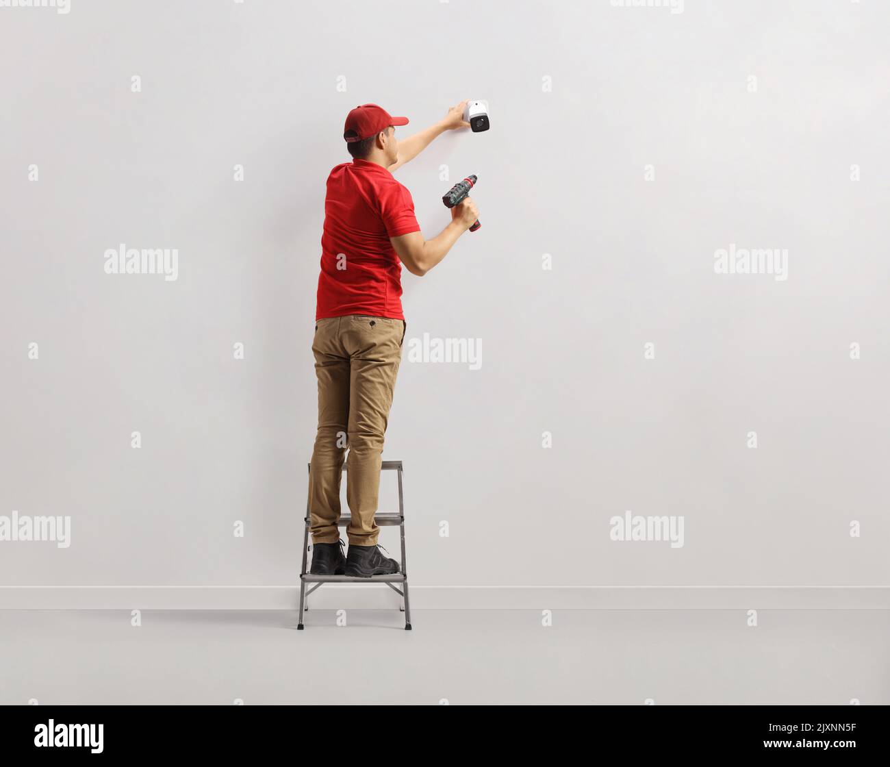 Worker standing on a ladder and installing a security camera on a wall ...