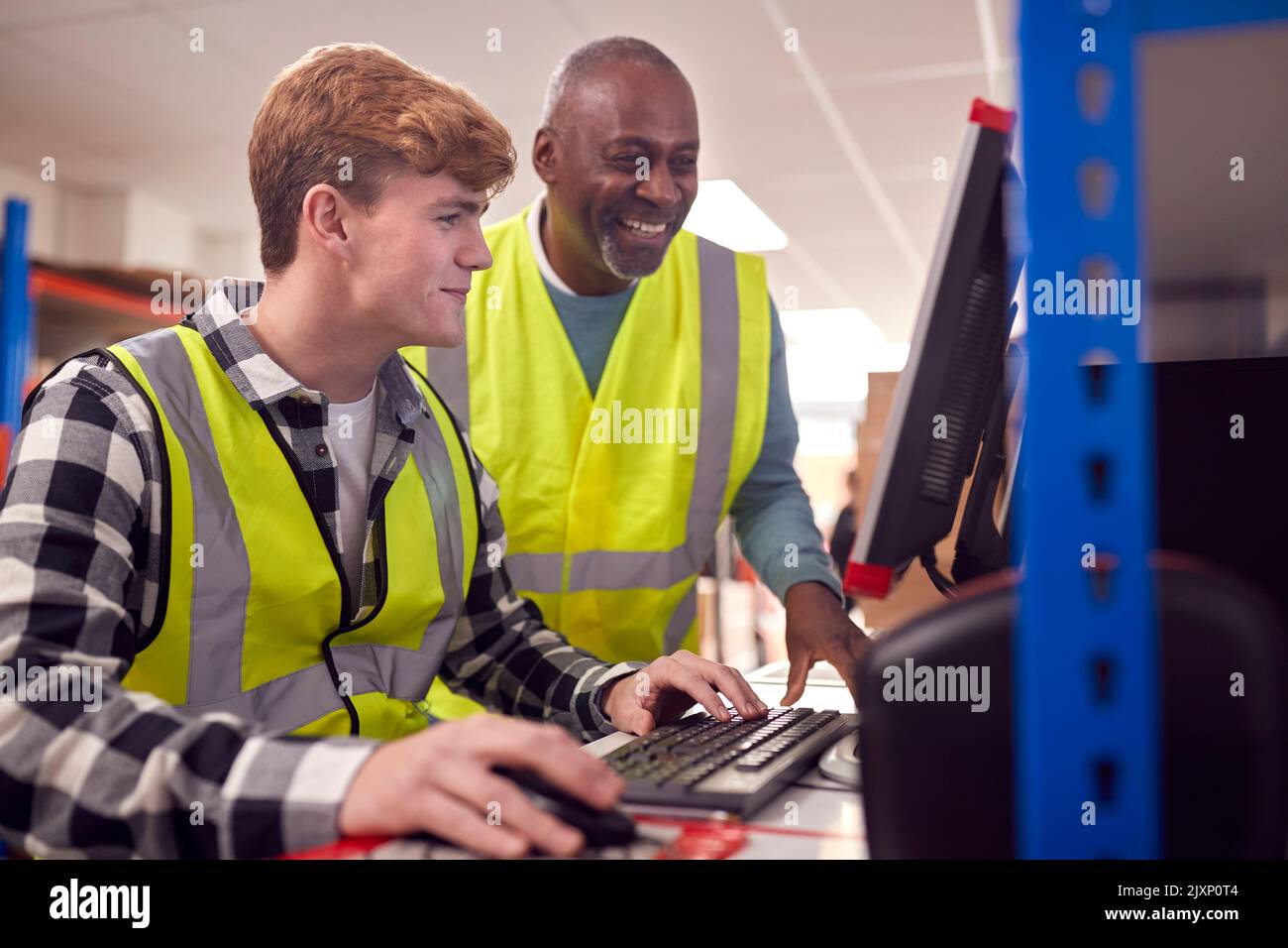 Male Intern With Supervisor Working In Busy Modern Warehouse On ...