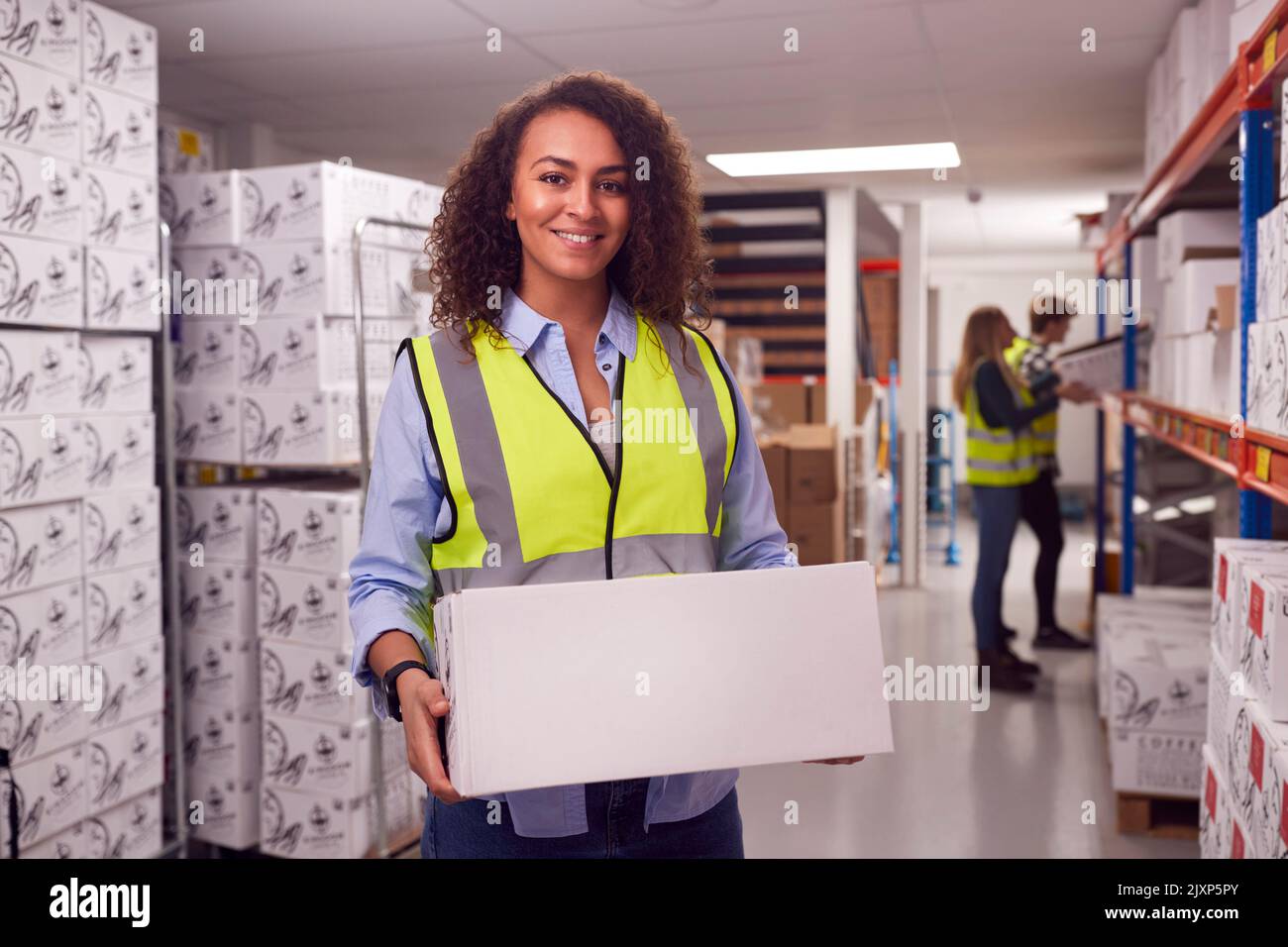 Portrait Of Female Worker Inside Busy Warehouse Carrying Box Stock ...