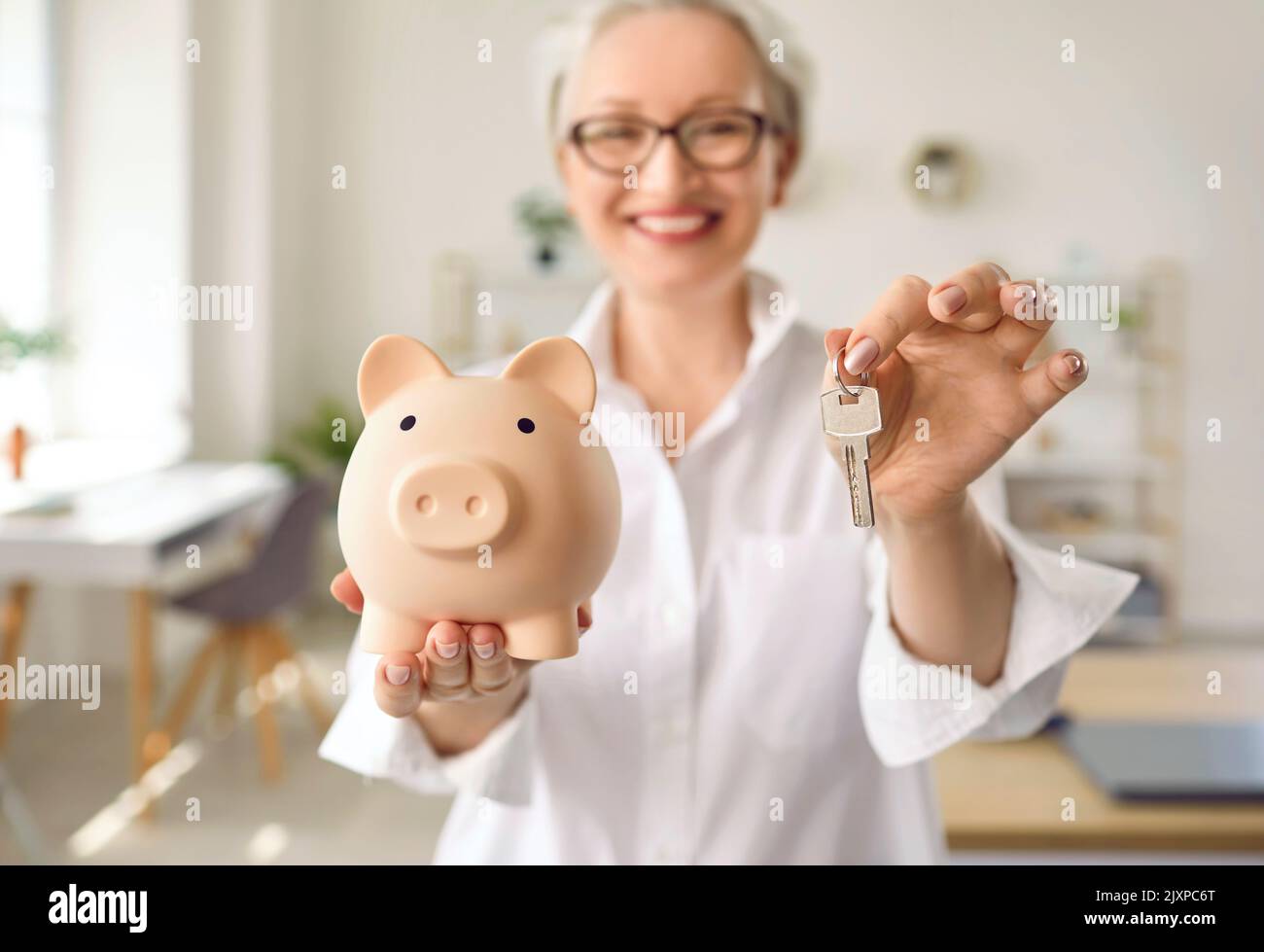 Happy woman who has saved money is holding a piggy bank and keys to her ...