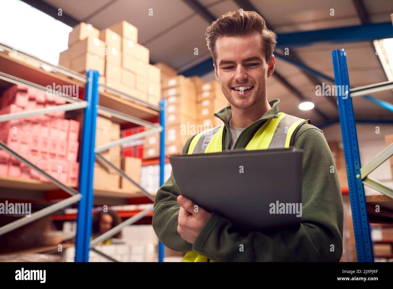 Male Worker Wearing High-Vis Vest Inside Busy Warehouse Checking Stock ...