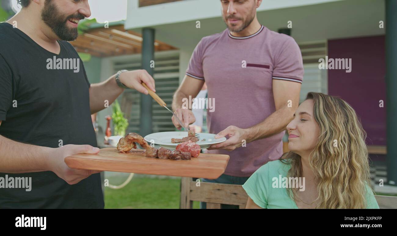 Group of friends having an outdoor barbecue. Man serves meat to friend ...
