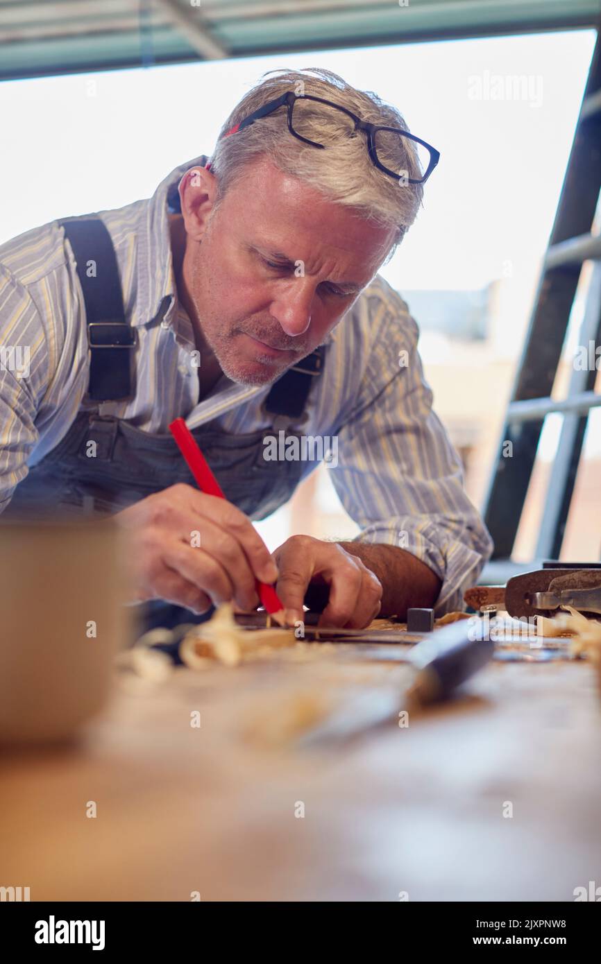 Mature Male Carpenter In Garage Workshop Marking Wood With Pencil And ...