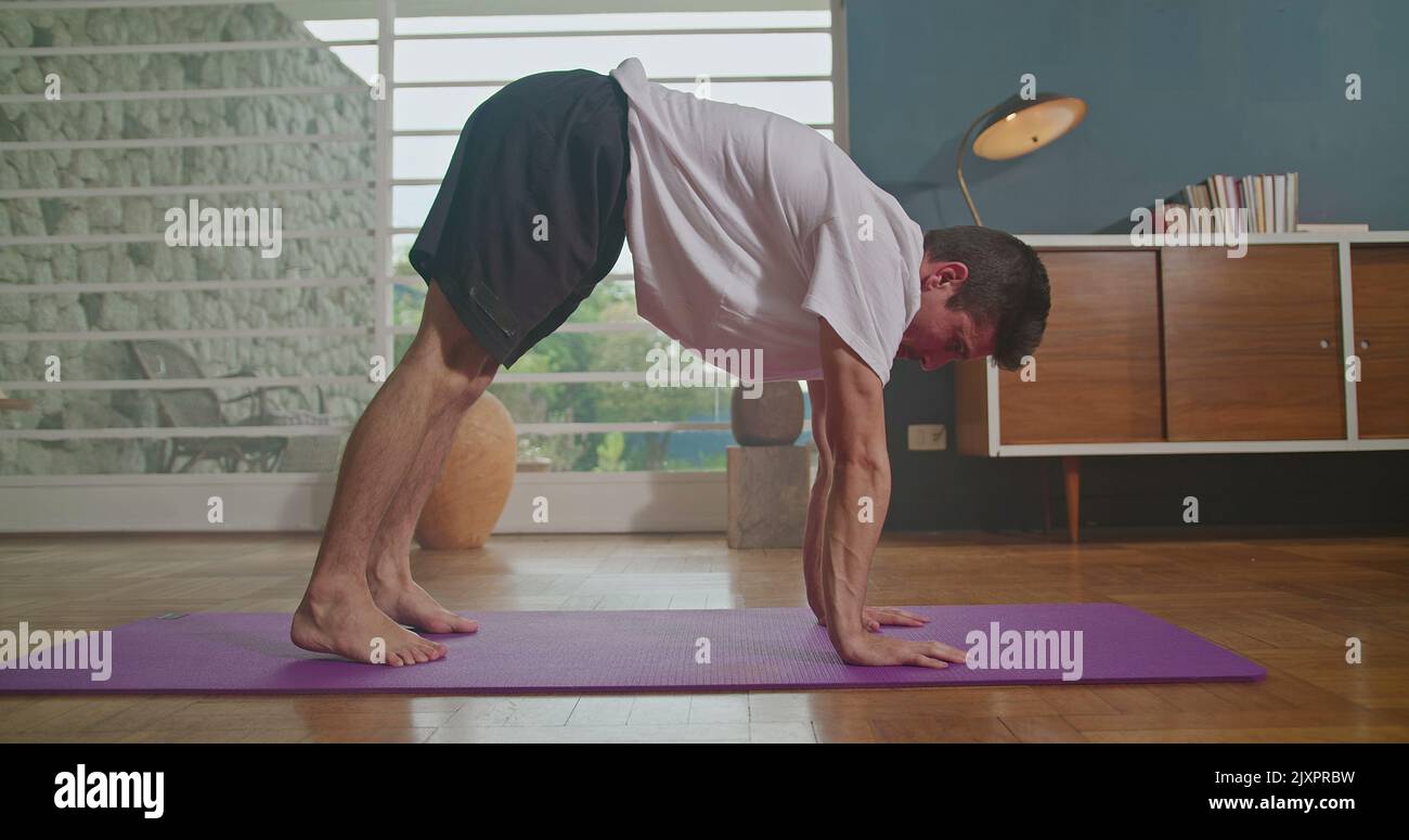 Man stretches on a mat in the living room and practices yoga. He does ...