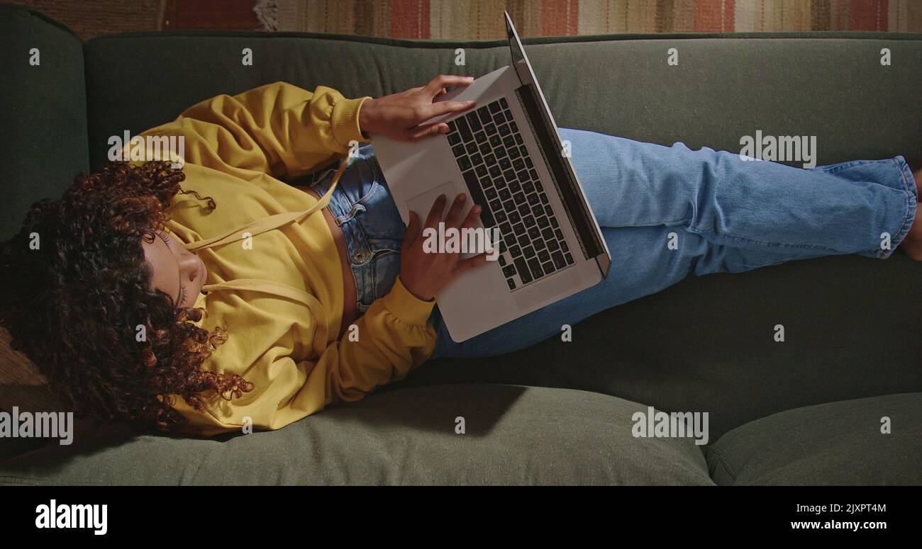 A young woman uses her laptop while sitting on comfortable sofa. A ...