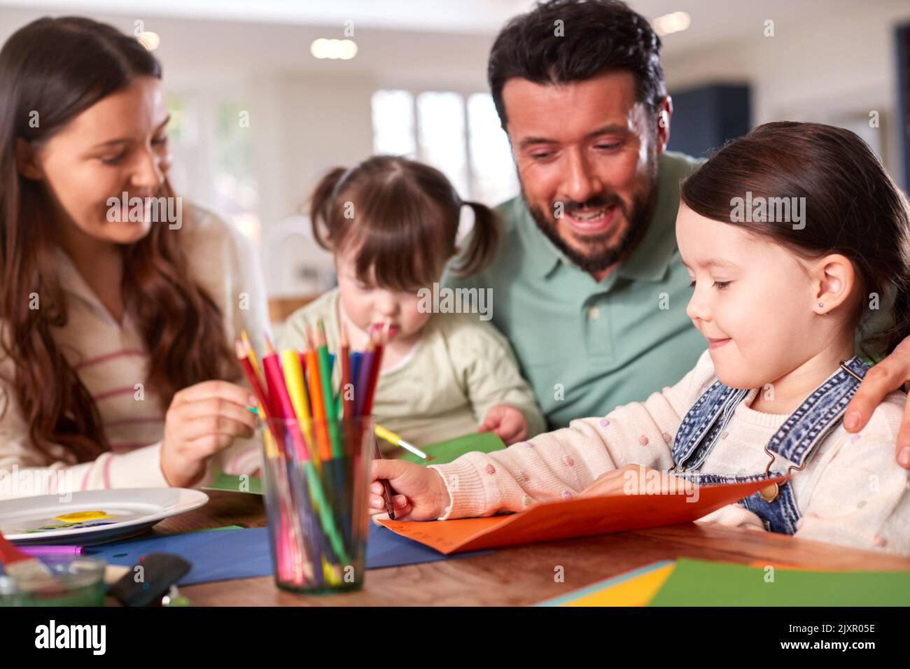 Family With Down Syndrome Daughter Sitting Around Table At Home Doing ...