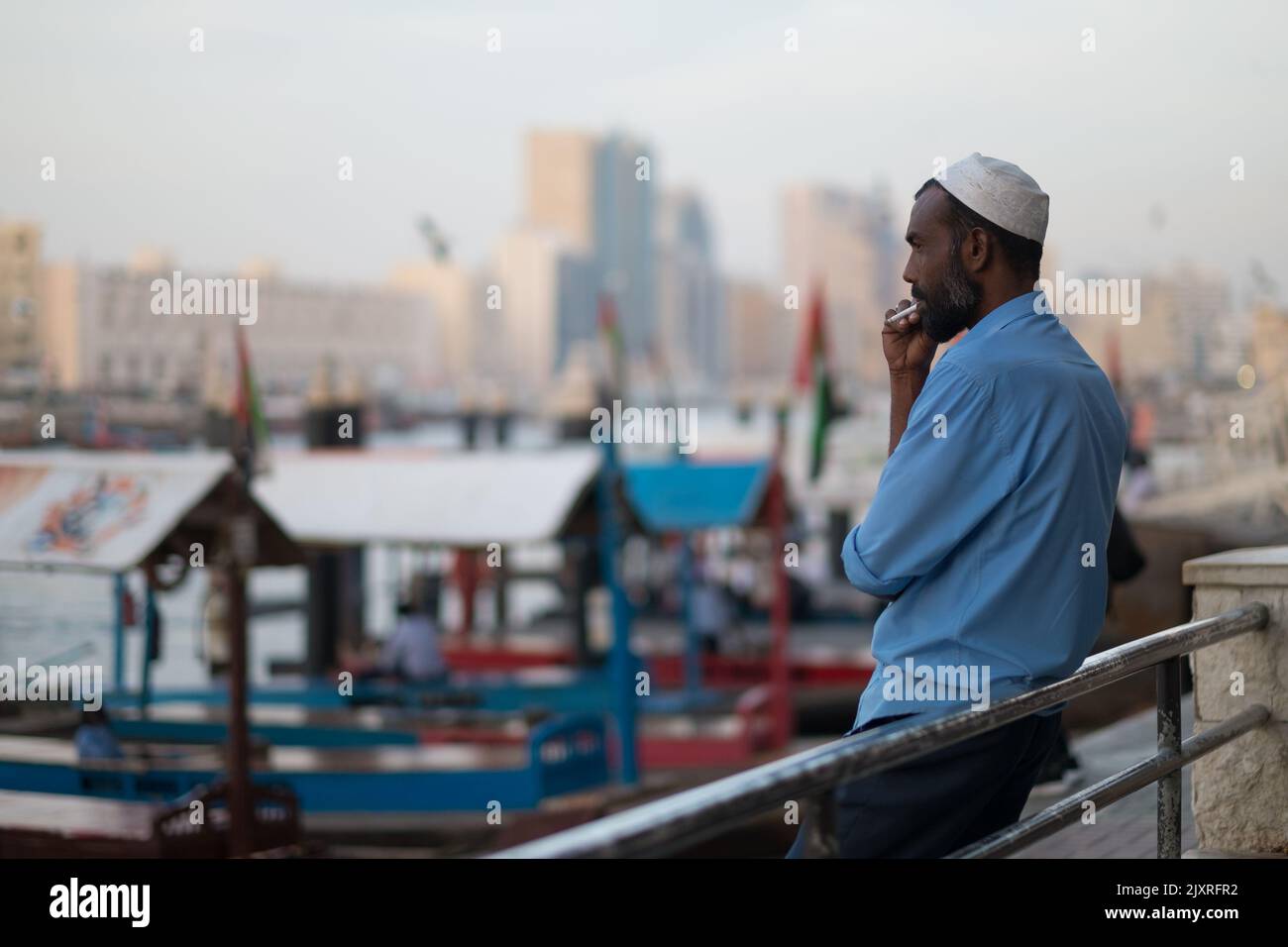A bearded man with Kufi leans on a railing with a cigarette between his ...