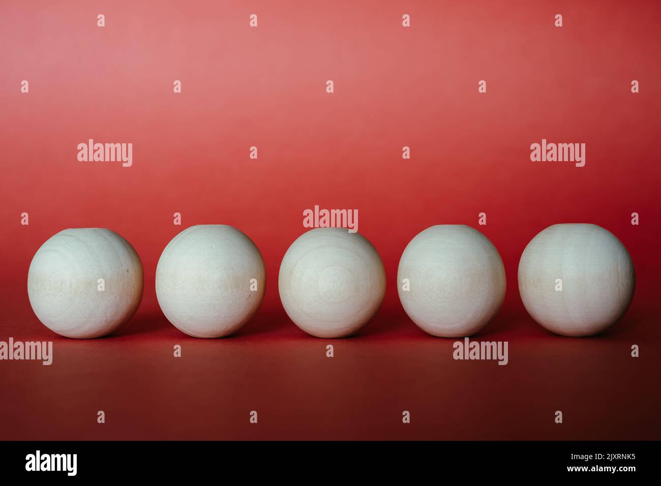View of five equidistant separated wooden balls on red background ...