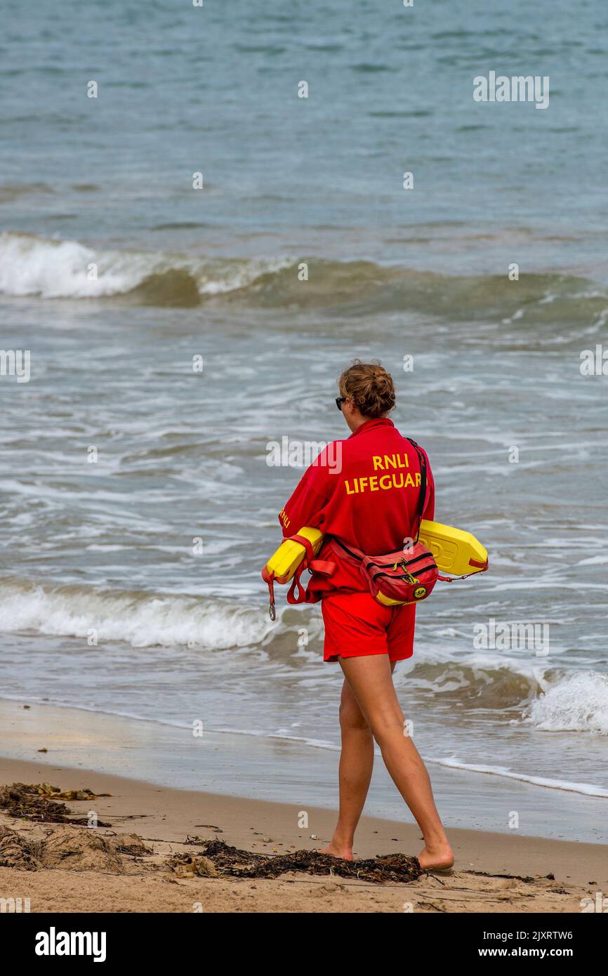 RNLI lifeguard walking along the beach at swanage in dorset, royal ...
