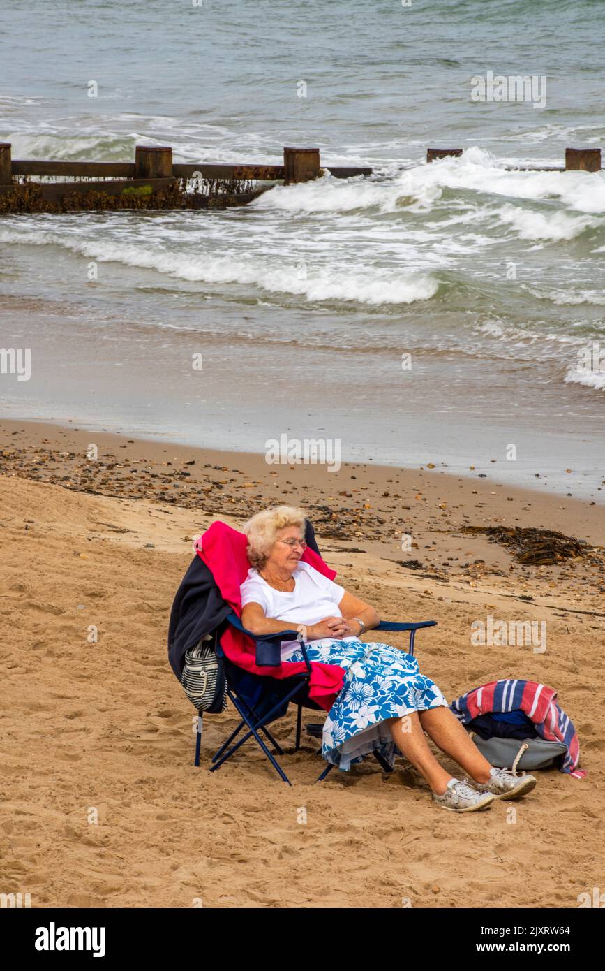 older lady falling asleep in a deckchair on a sandy beach at swanage ...