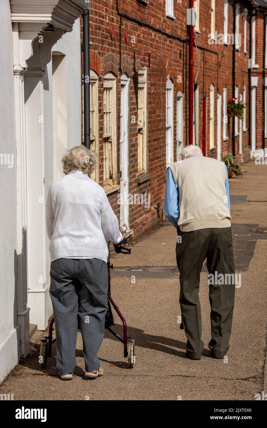 elderly couple walking along a pavement at the side of the road, old ...