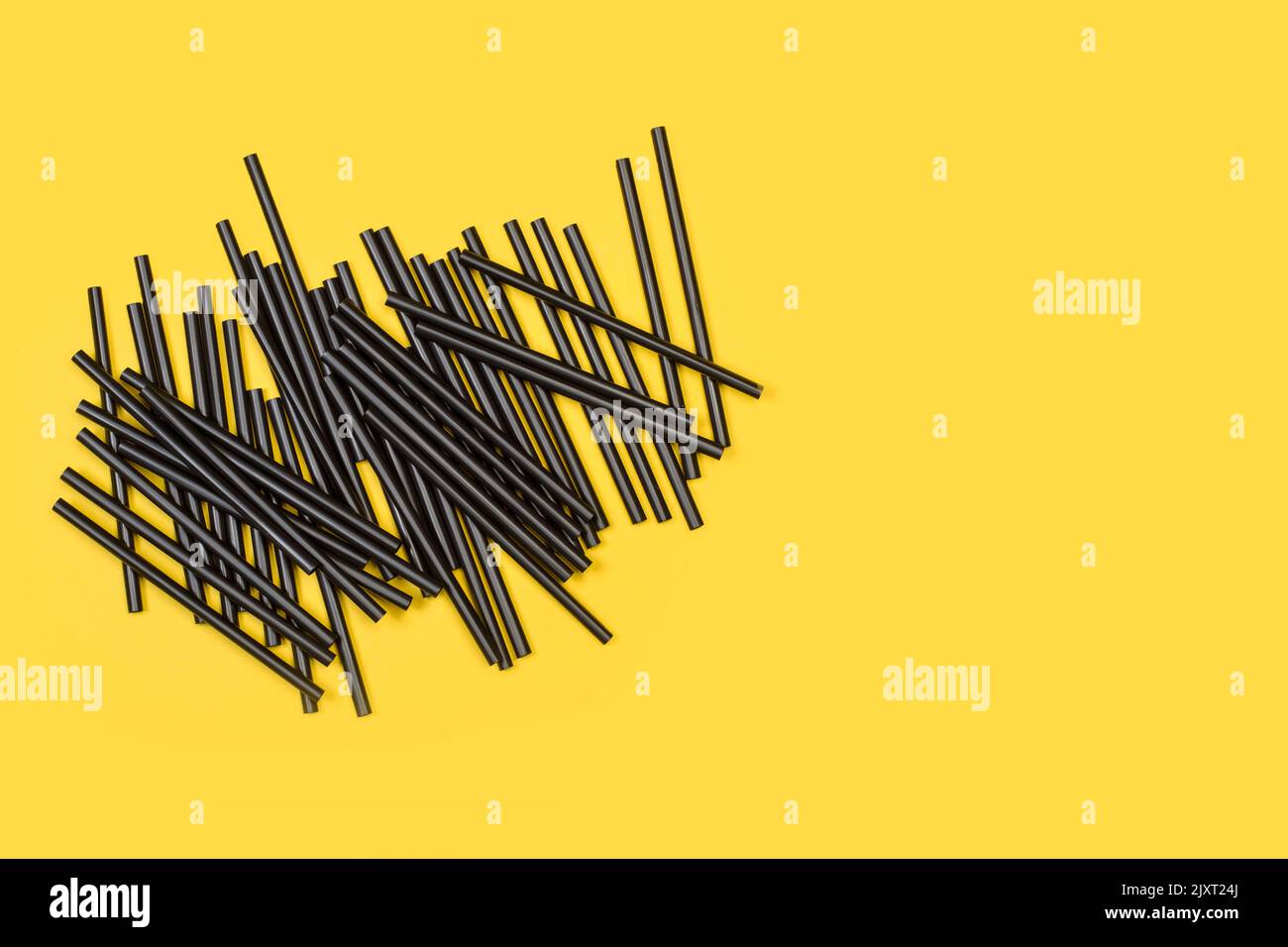 A lot of black plastic straws on a yellow background with copy space ...