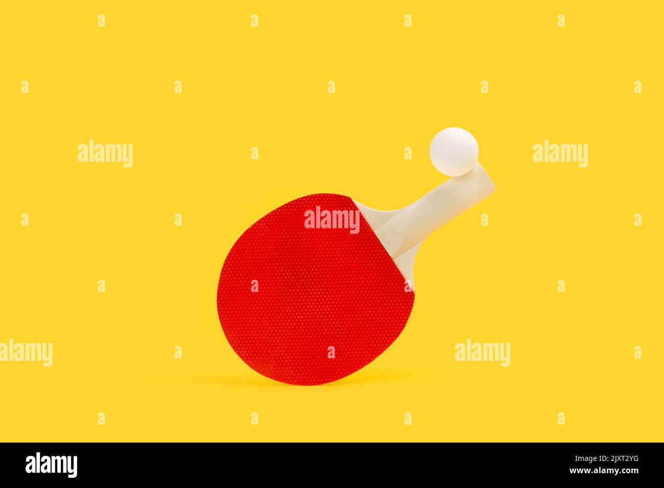 Red ping pong paddle and a white ball on a yellow background with copy ...