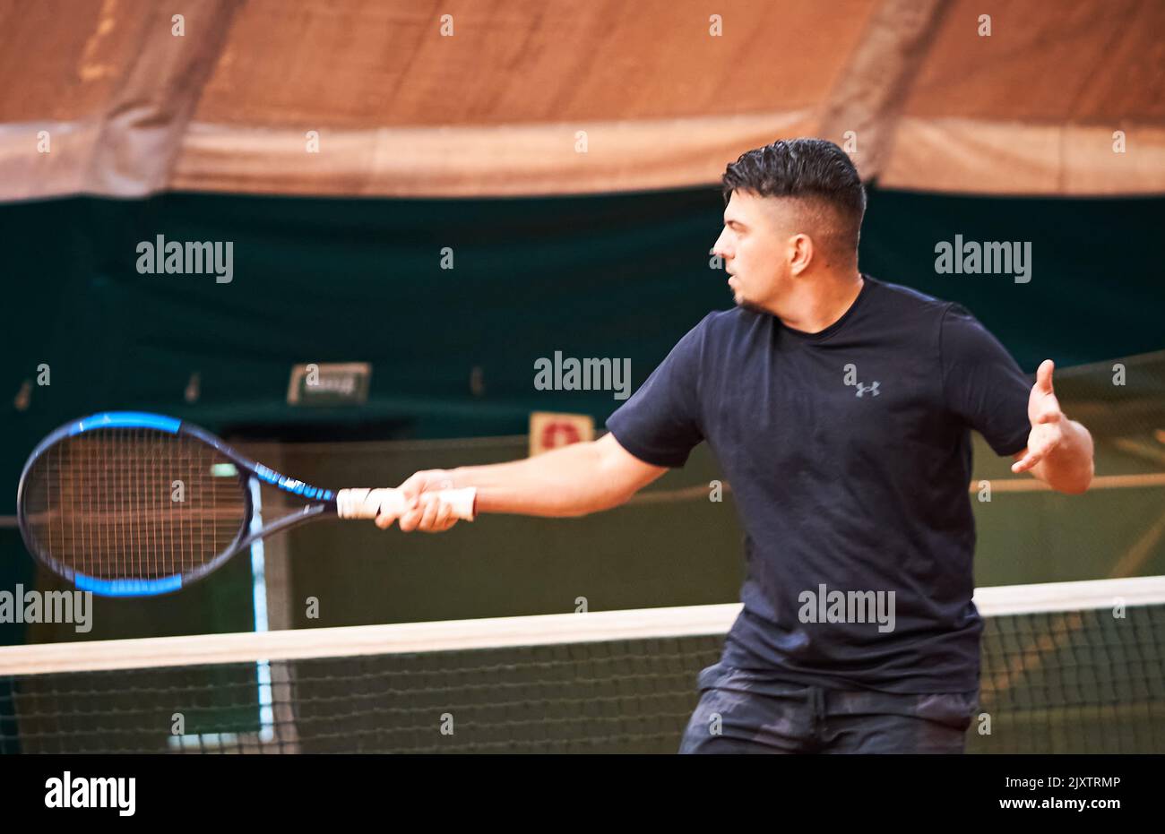 Young man playing tennis with friend and serving ball, view from back ...