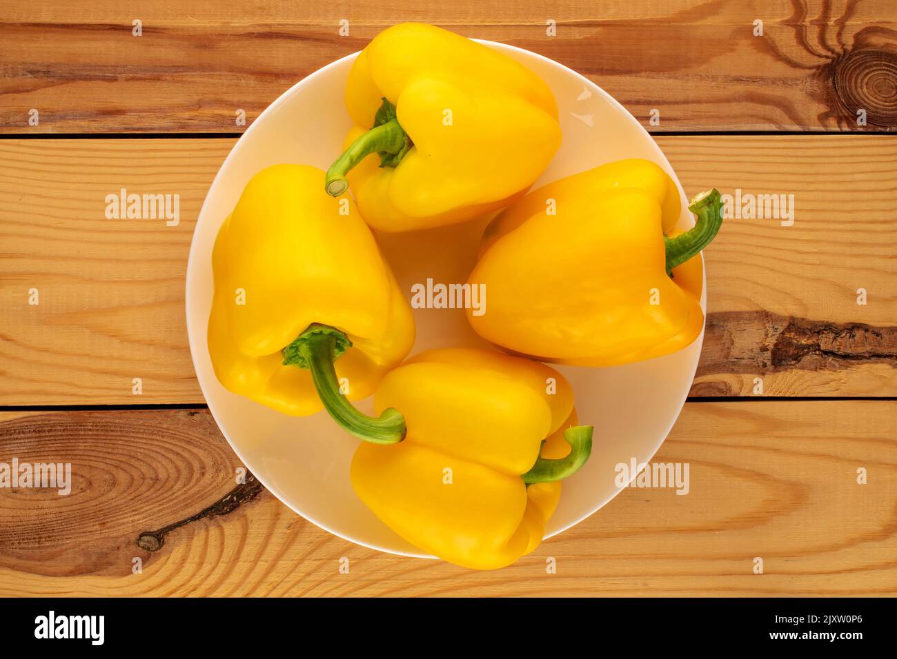 Four ripe yellow sweet peppers with a ceramic plate on a wooden table ...