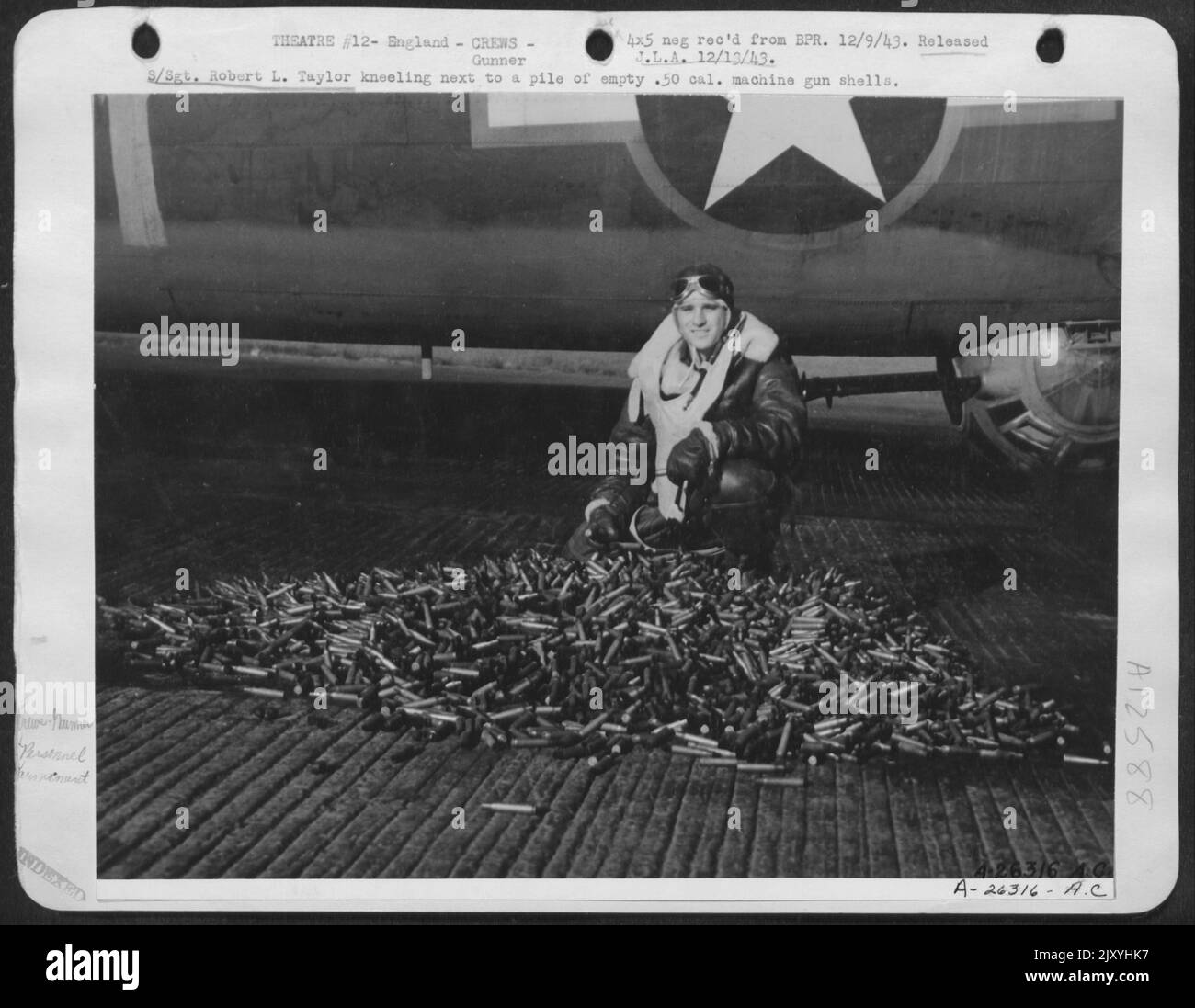 S/Sgt. Robert L. Taylor kneeling next to a pile of empty .50 cal ...