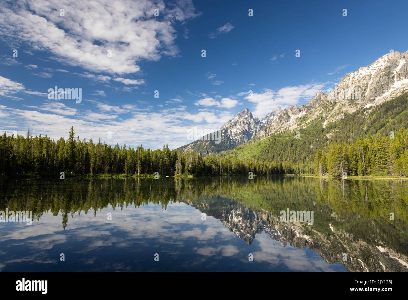 Passing clouds reflected in the calm morning waters of String Lake ...