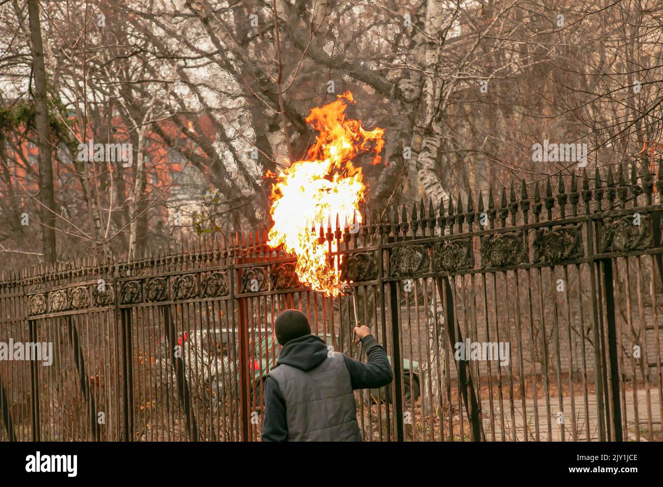 A worker cleans old paint from a metal fence using fire. A man holds a ...