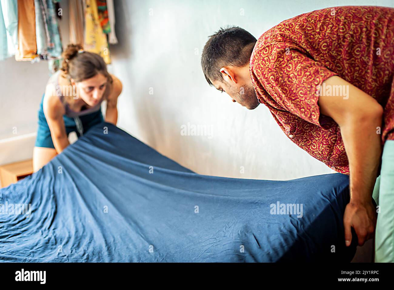 Cheerful young couple making bed, having fun at home. Doing house ...