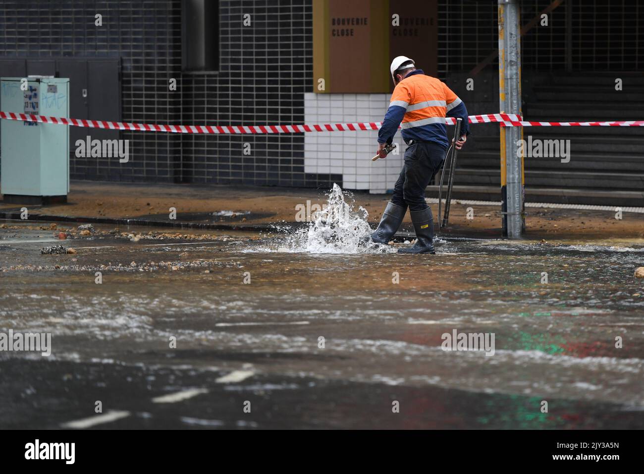 A worker cleans up after a burst water pipe flooded Victoria street in ...