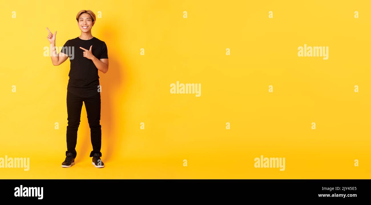 Full-length of smiling attractive korean guy pointing fingers left ...