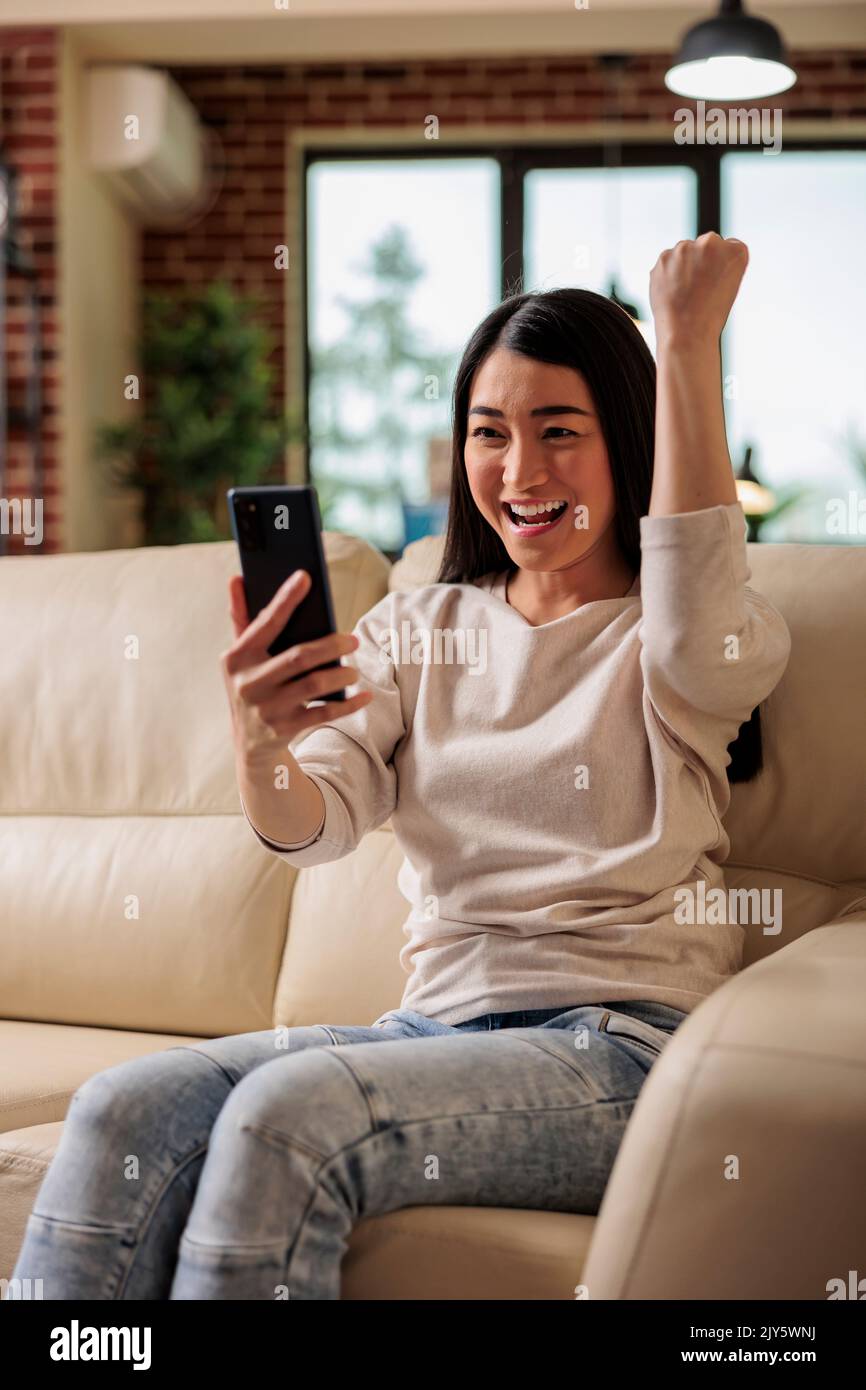 Authentic looking asian woman playing mobile online video games on phone winning and happy ...