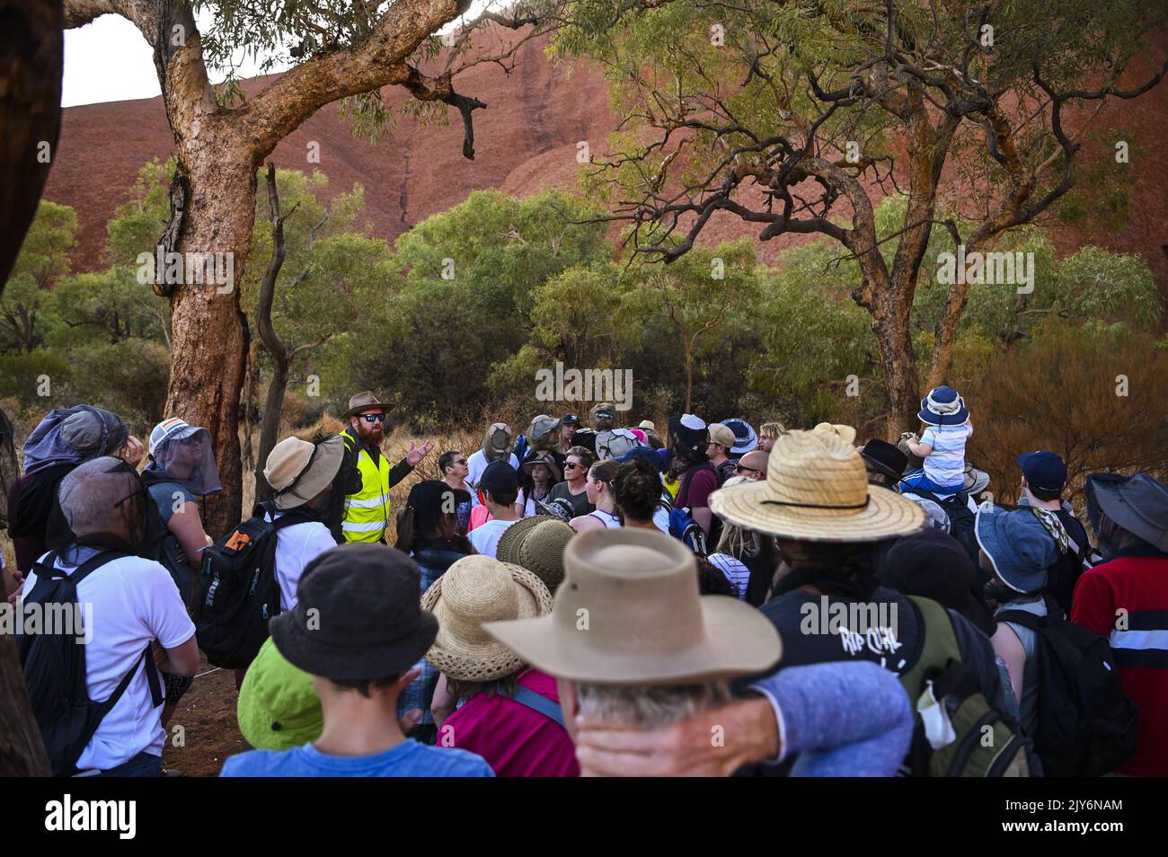 A tour guide speaks to tourists at the bottom of Uluru, also known as ...