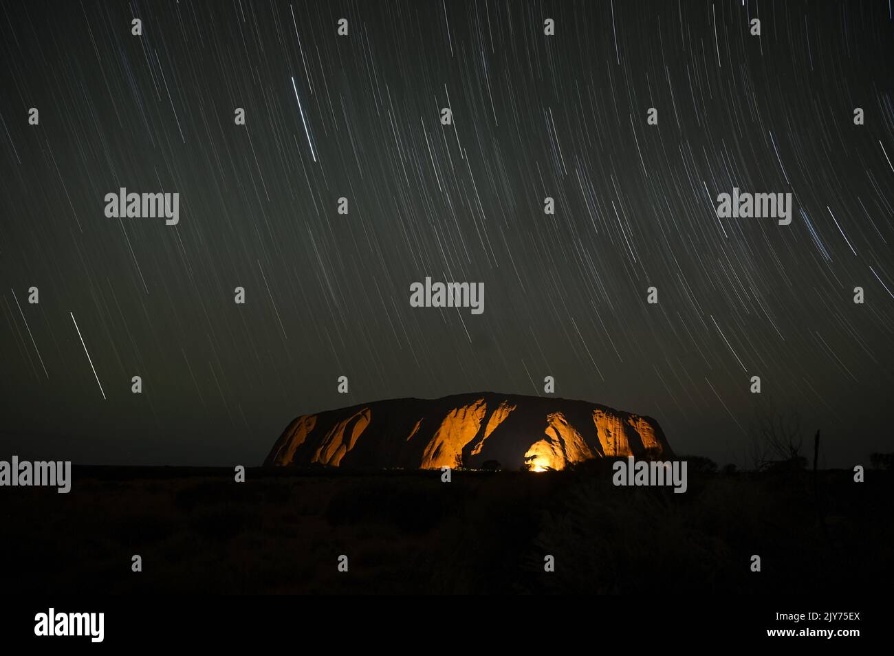 A long-exposure photograph shows star trails over Uluru, also known as ...
