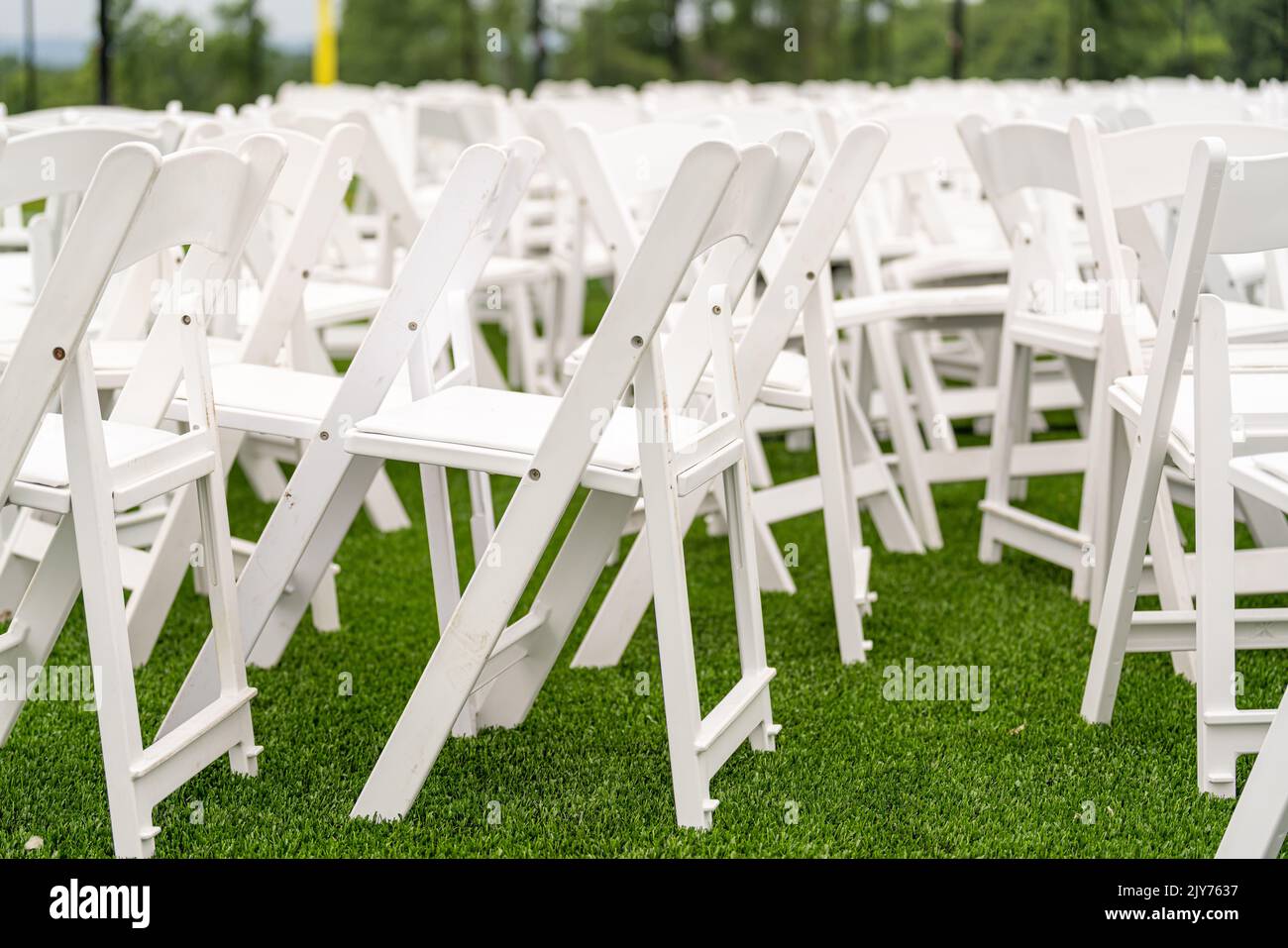 White chairs set-up in rows on a green synthetic turf athletic field ...