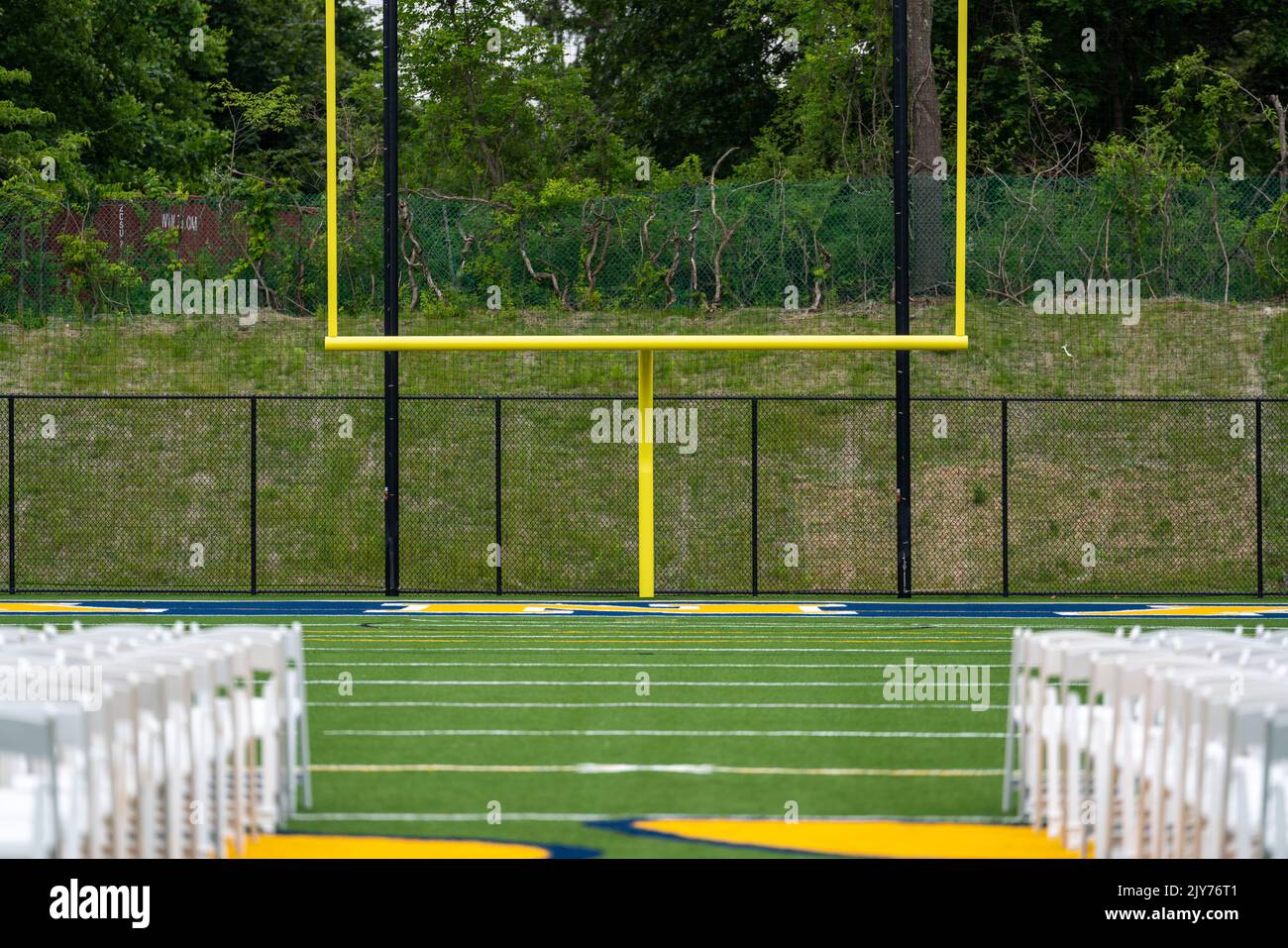 White chairs set-up in rows on a green synthetic turf athletic field for a high school ...