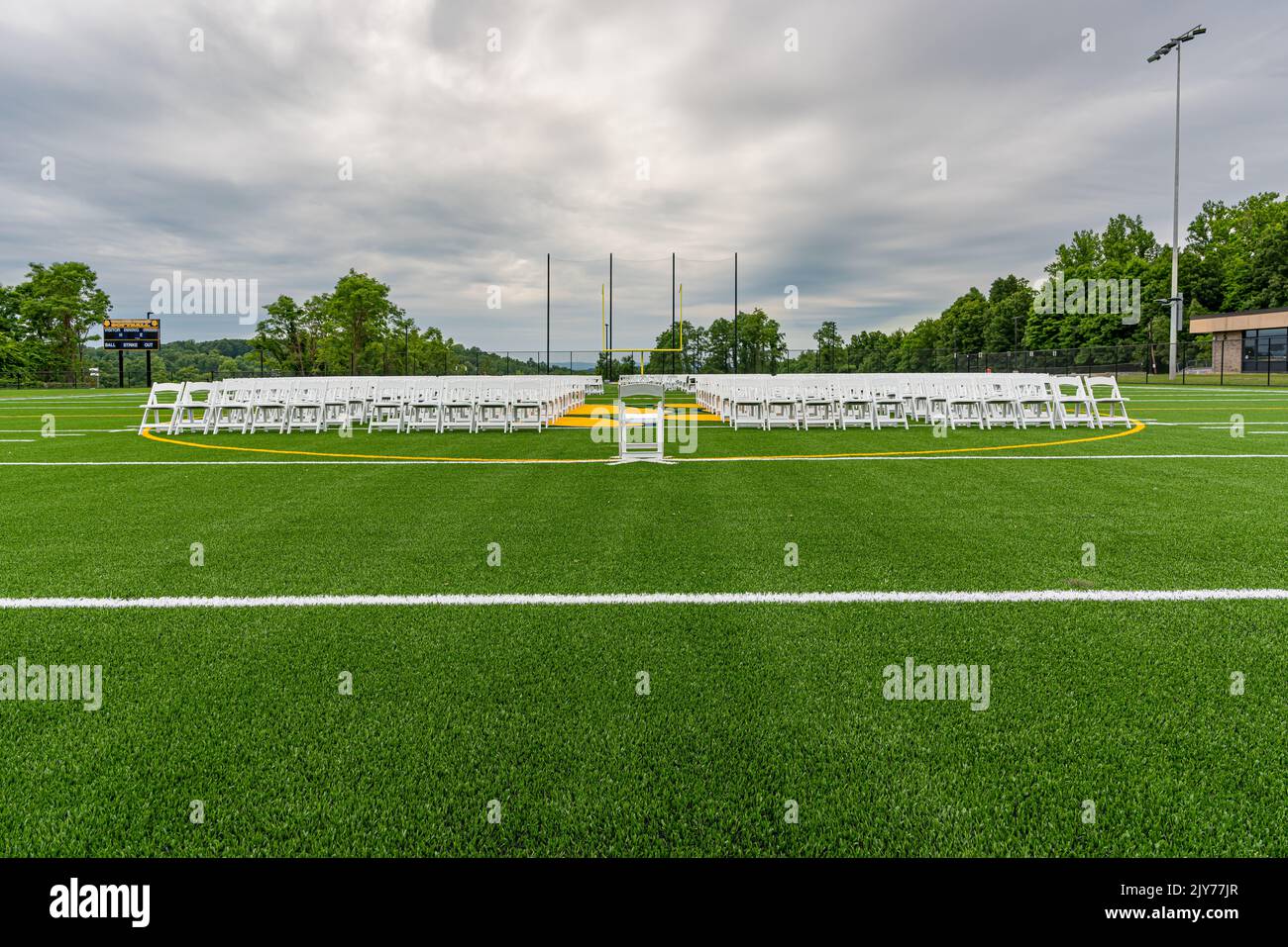 White chairs set-up in rows, with single chair at center, on a green ...