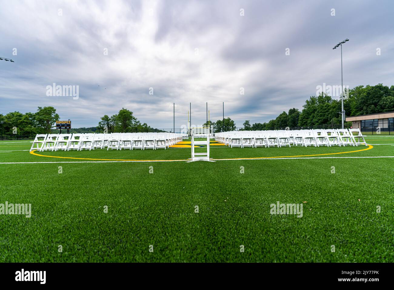 White chairs set-up in rows, with single chair at center, on a green ...