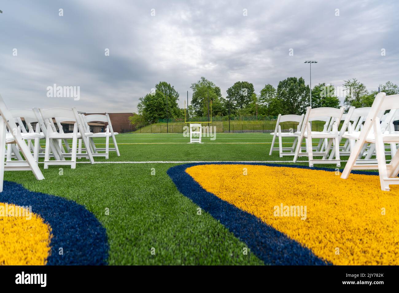 White chairs set-up in rows, with single chair at center, on a green ...
