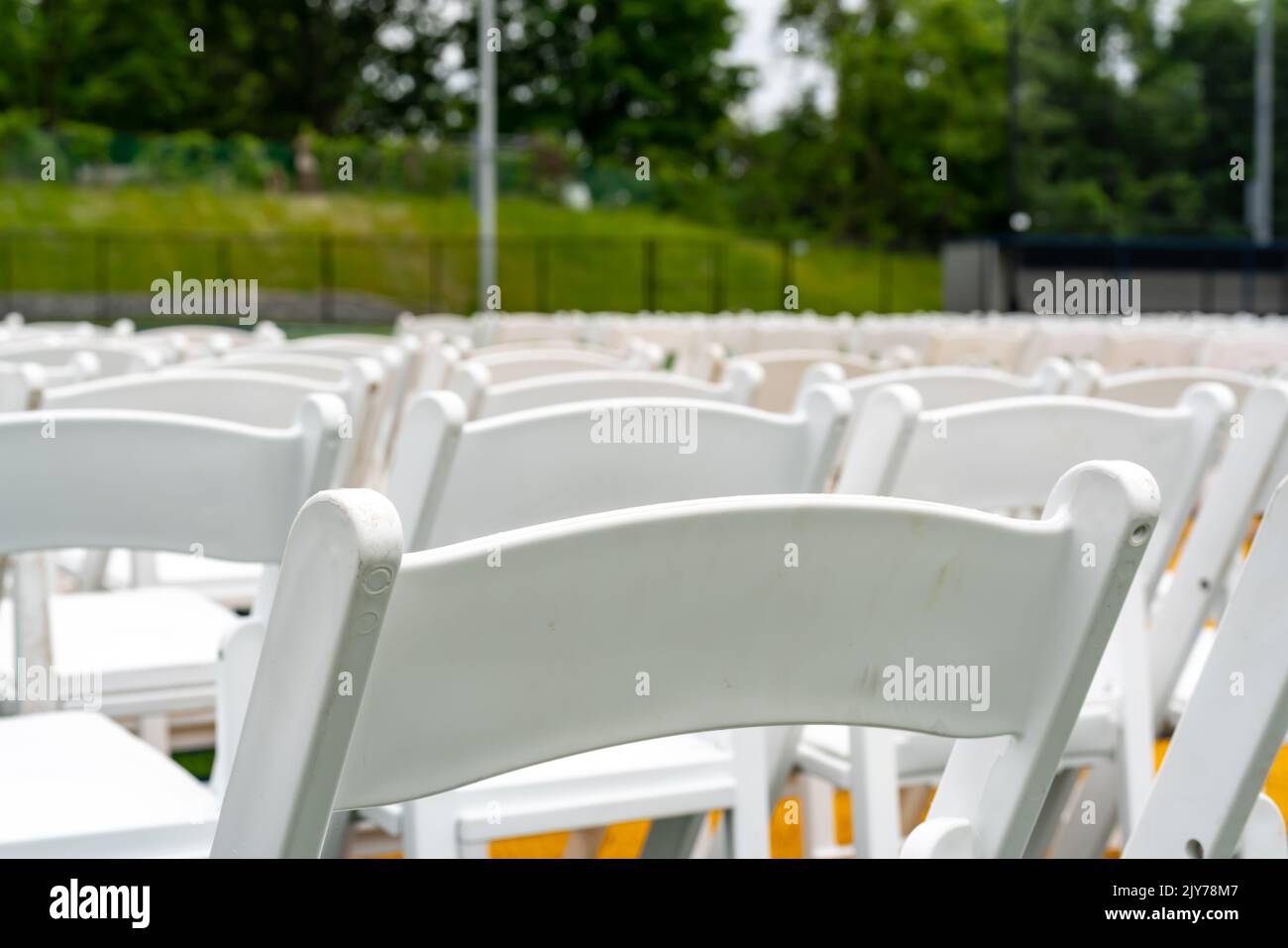 White chairs set-up in rows on a green synthetic turf athletic field ...