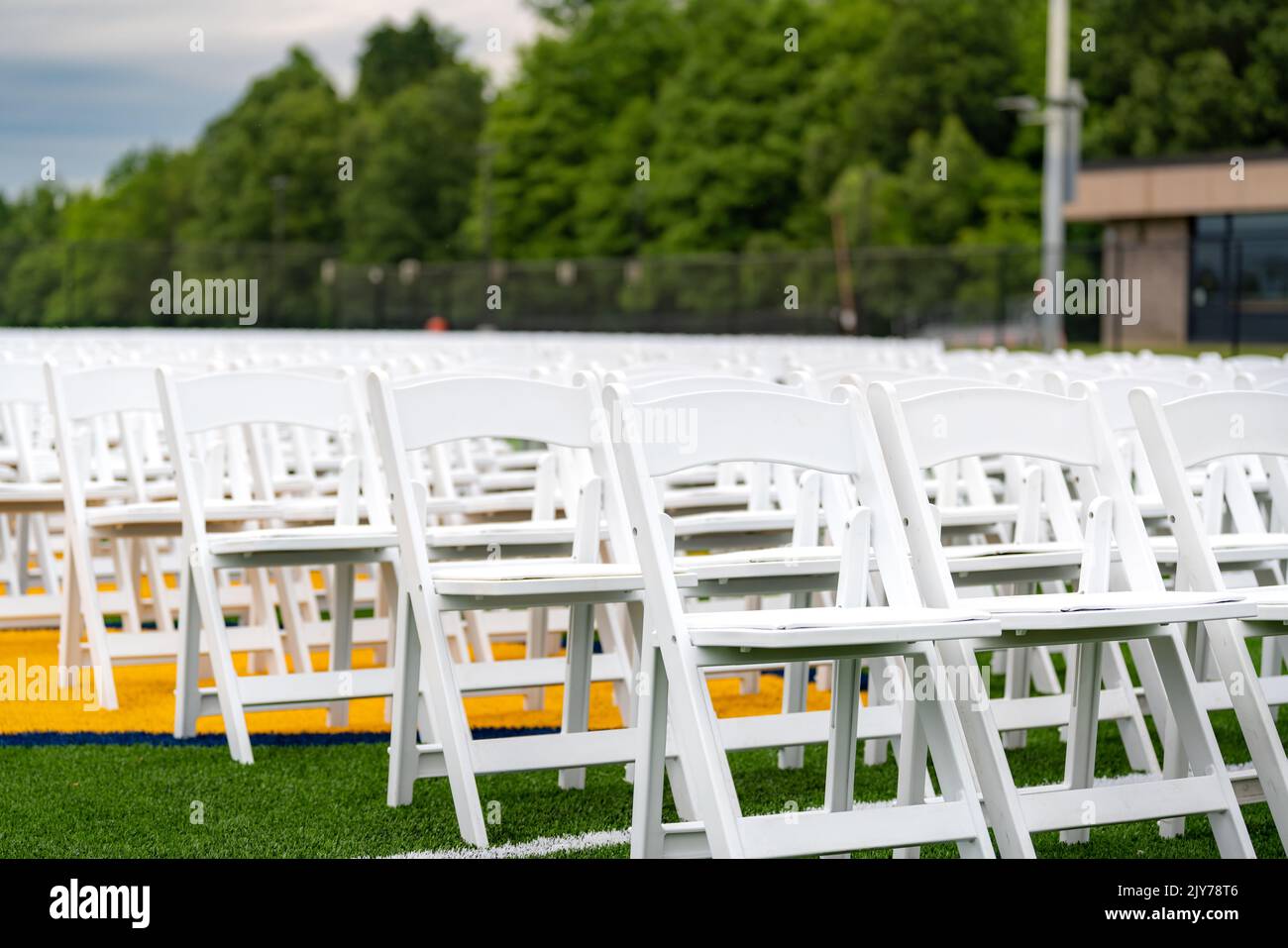 White chairs set-up in rows on a green synthetic turf athletic field ...