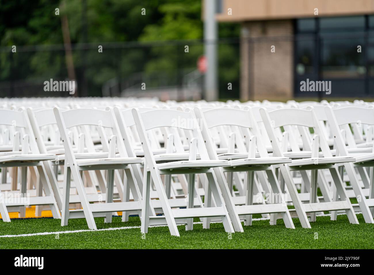 White chairs set-up in rows on a green synthetic turf athletic field ...