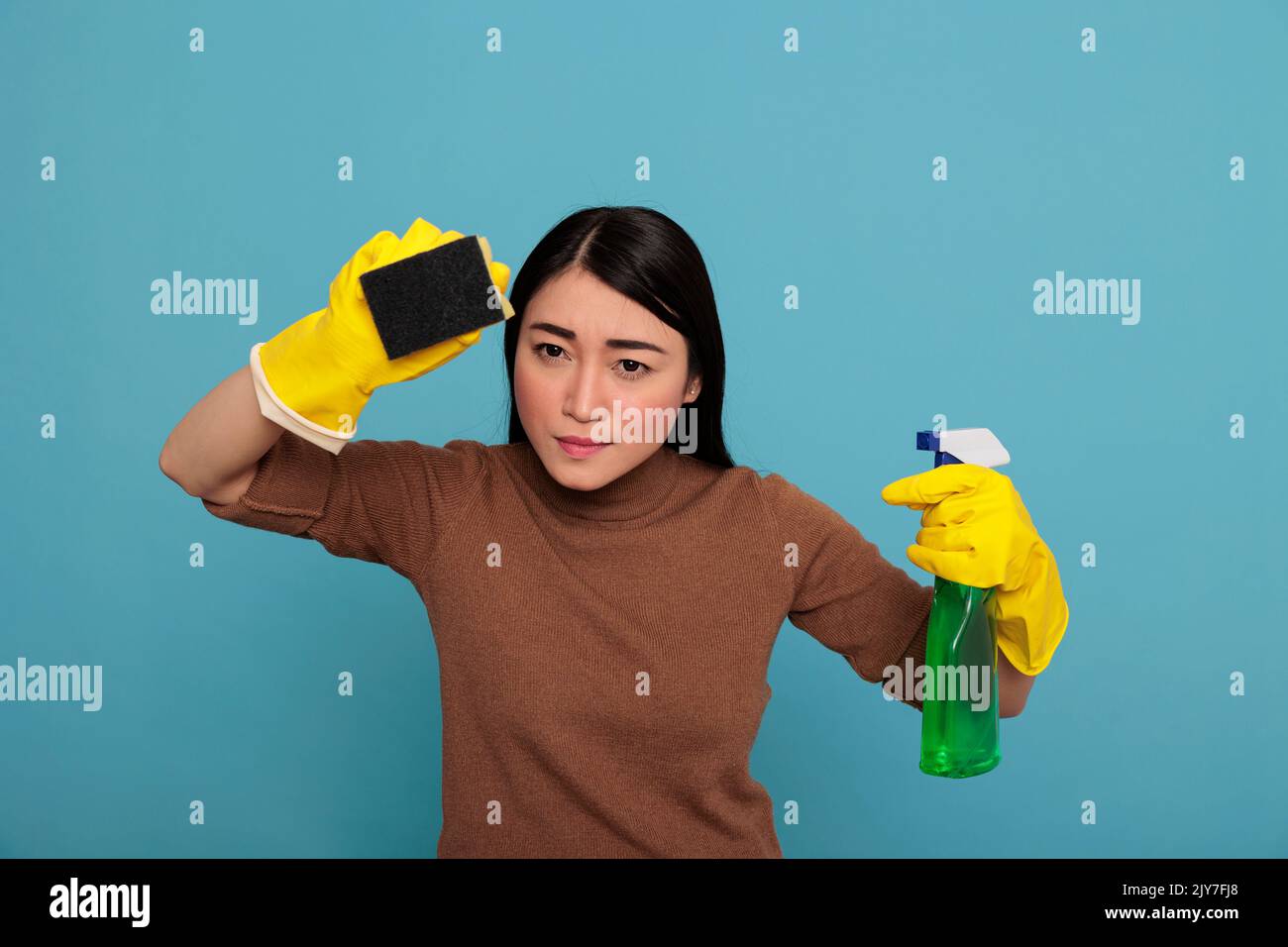 Portrait of serious young woman wearing yellow gloves holding a sponge ...