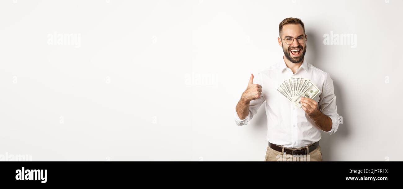 Excited rich man holding money, showing thumb up in approval, standing ...