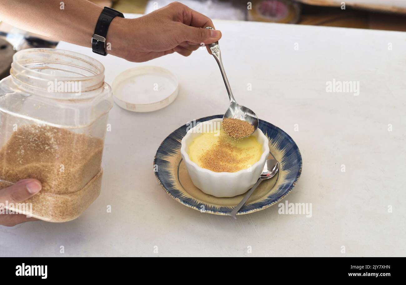 Process of sprinkling brown sugar on the Creme brulee on white ...