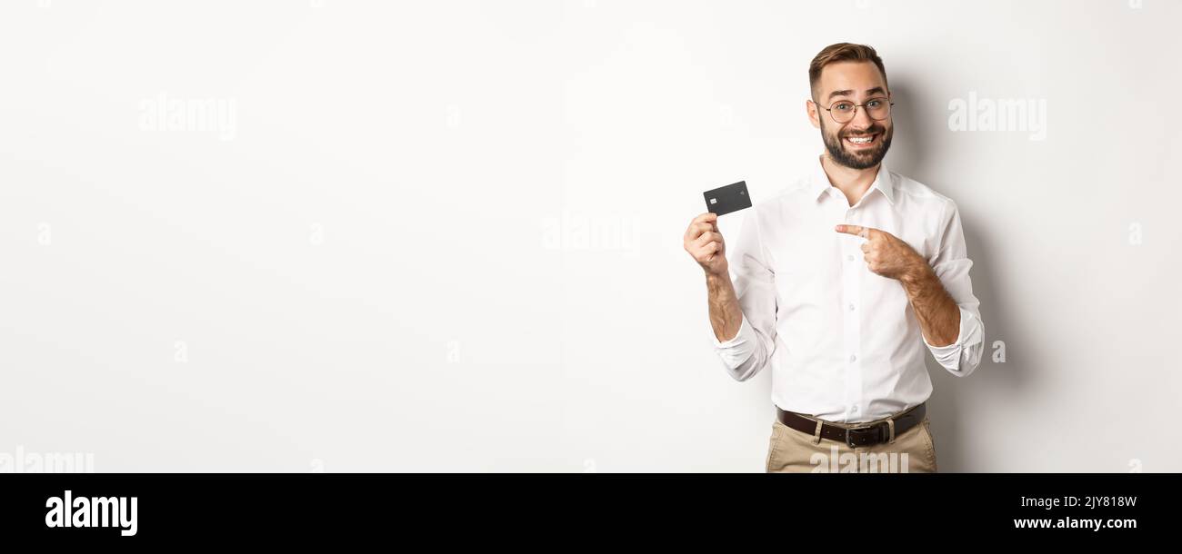 Handsome satisfied man in glasses pointing at credit card, pleased with ...