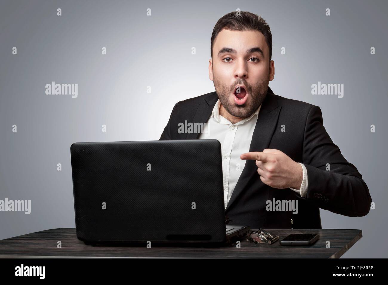 Surprised person, sitting behind his desk, pointing at laptop, isolated ...