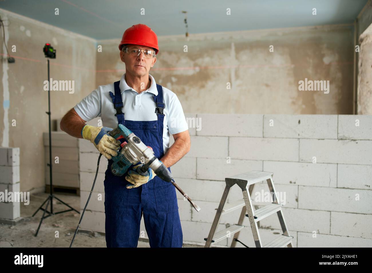 Professional construction worker in uniform standing with rotary hammer ...