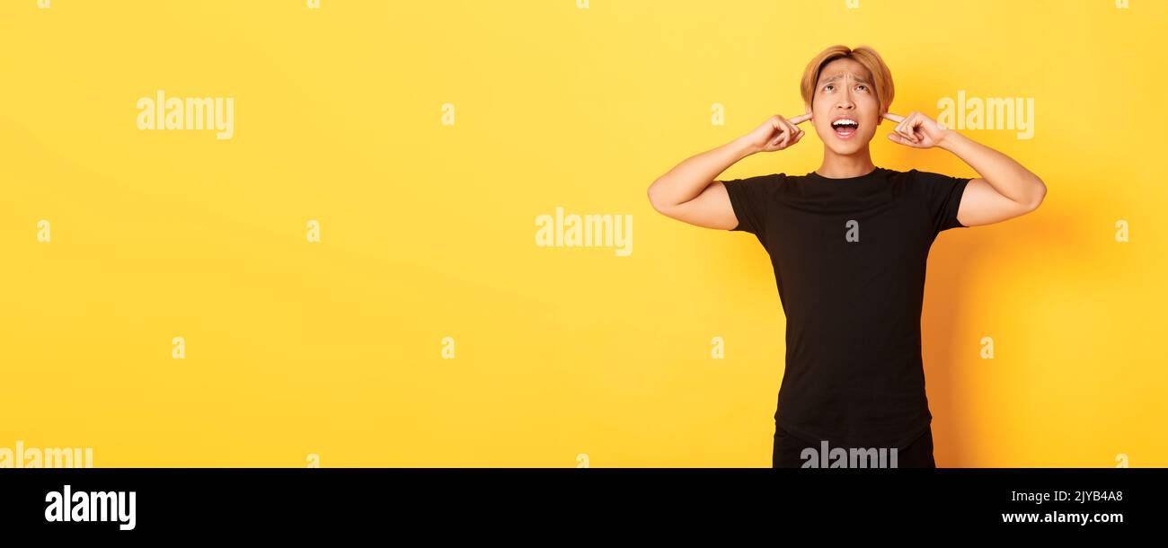 Portrait of annoyed and bothered asian guy grimacing, shut ears ...