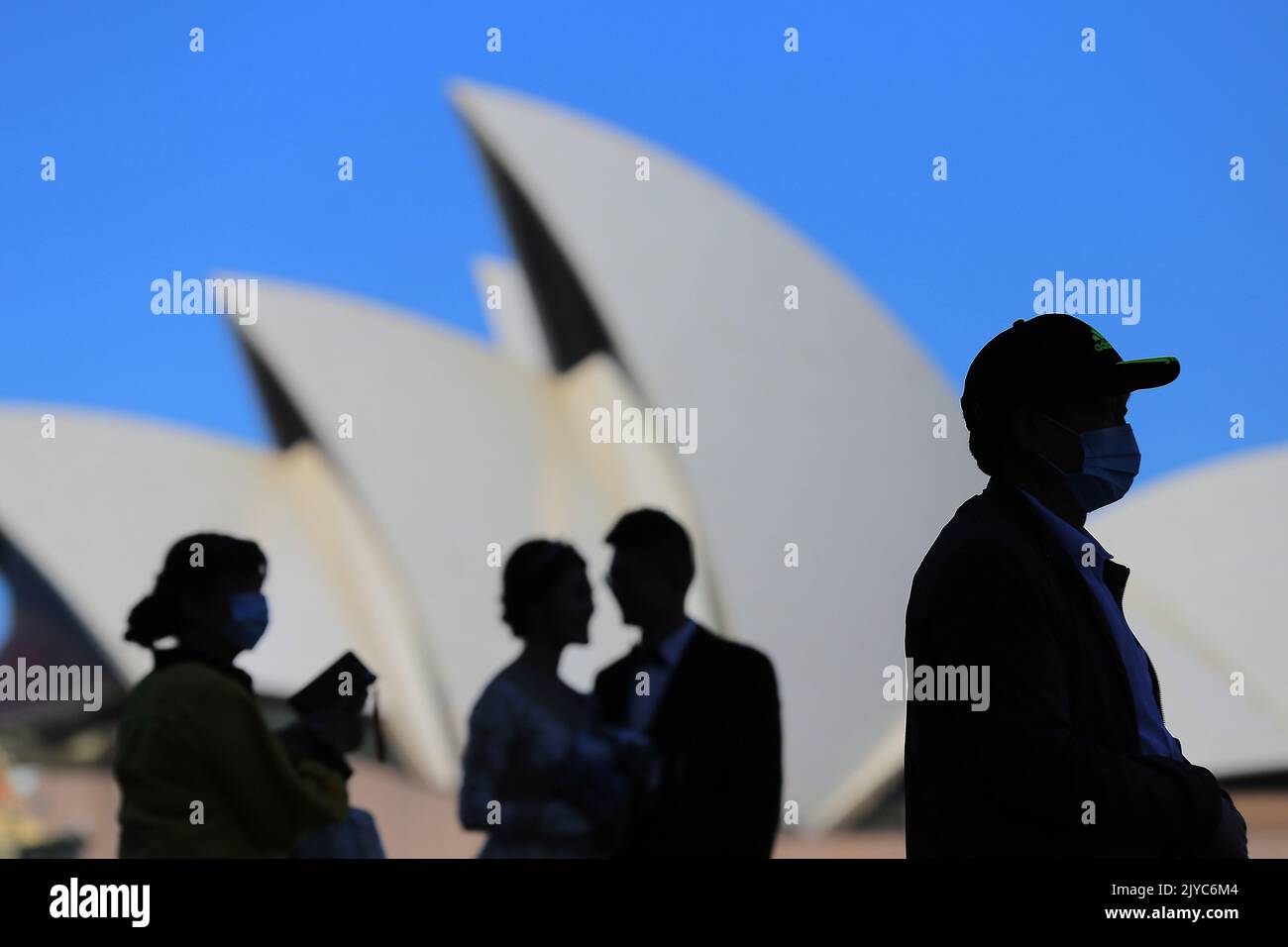 People wear face masks in front of the Sydney Opera House in Sydney ...