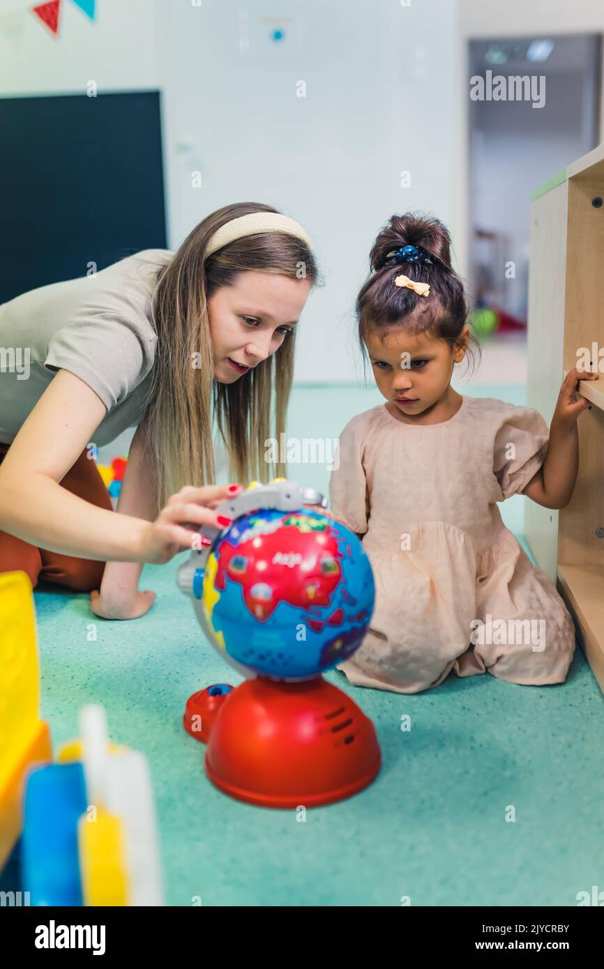 Playtime at nursery school. Toddler girl with her teacher playing with ...